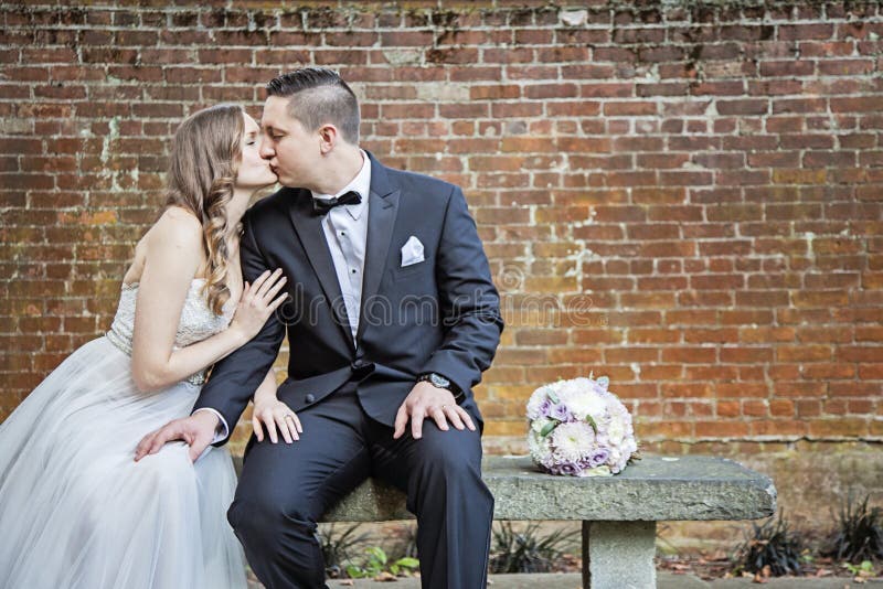 Bride and Groom Sitting on Bench in Front of Brick Wall Stock Photo ...