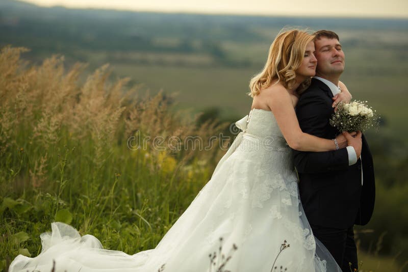 Bride Hugs Groom from Behind while they Daydreams on a Hill Stock Image ...