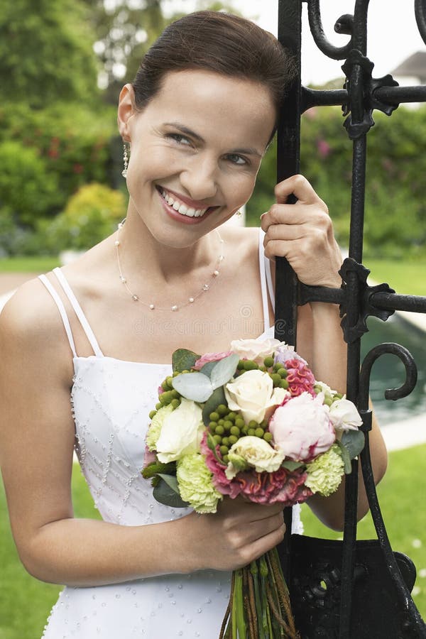 Bride Leaning on Garden Gate Holding Bouquet Stock Image - Image of ...