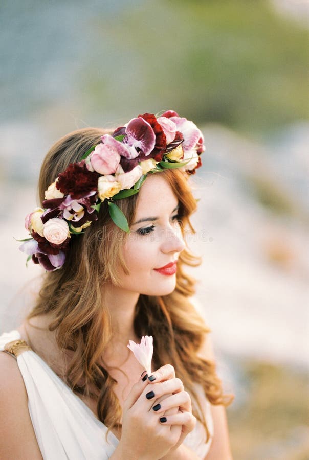Bride in a Multi-colored Wreath Holds a Flower in Her Hands in Front of ...