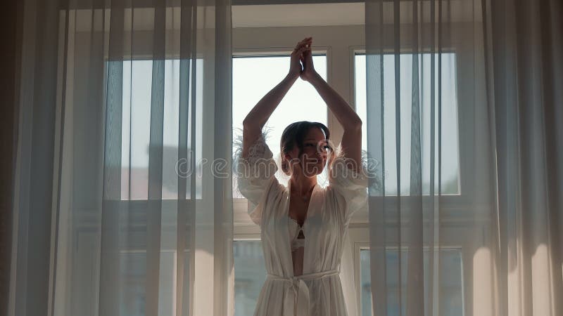 Bride Posing Gracefully with Arms Raised by Window, a Bride Poses with ...