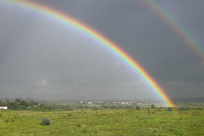Bright Double Rainbow Rising from a Meadow with Dark Rain Clouds in the ...