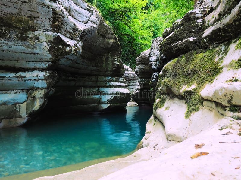 A Bright Turquoise Calm River Flows between Mossy Rocks with Bright ...