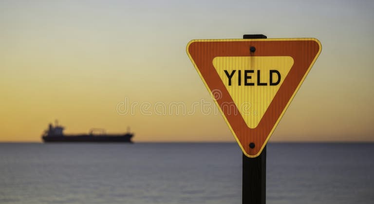 Bright Yellow Triangular YIELD Sign on Pole Against Calm Ocean and ...
