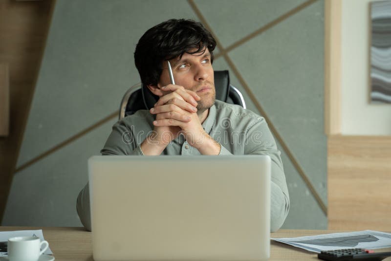 Brooding Young Man Holding Pen in Hand and Looking Away while Sitting ...