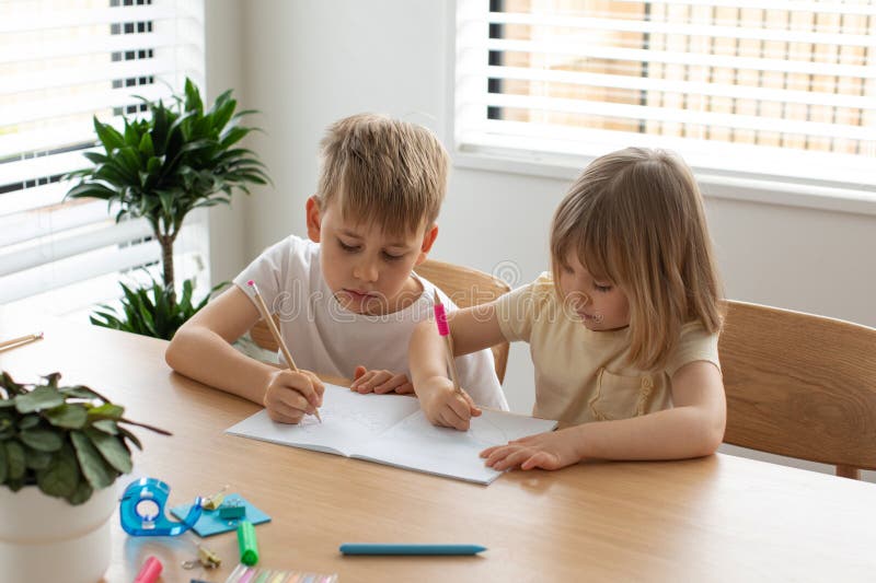 Brother and Sister Write and Draw Together with Pencils at the Table ...
