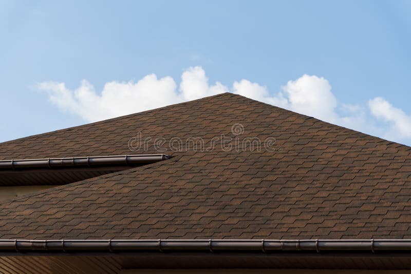 A Brown Shingle Roof with a Brown Gutter Against a Blue Sky with Some ...