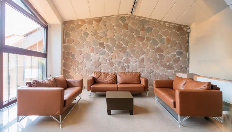 Brown Sofas Against Stone Tiles Cladding Wall in Room with High Ceiling ...
