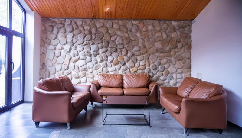 Brown Sofas Against Stone Tiles Cladding Wall in Room with High Ceiling ...