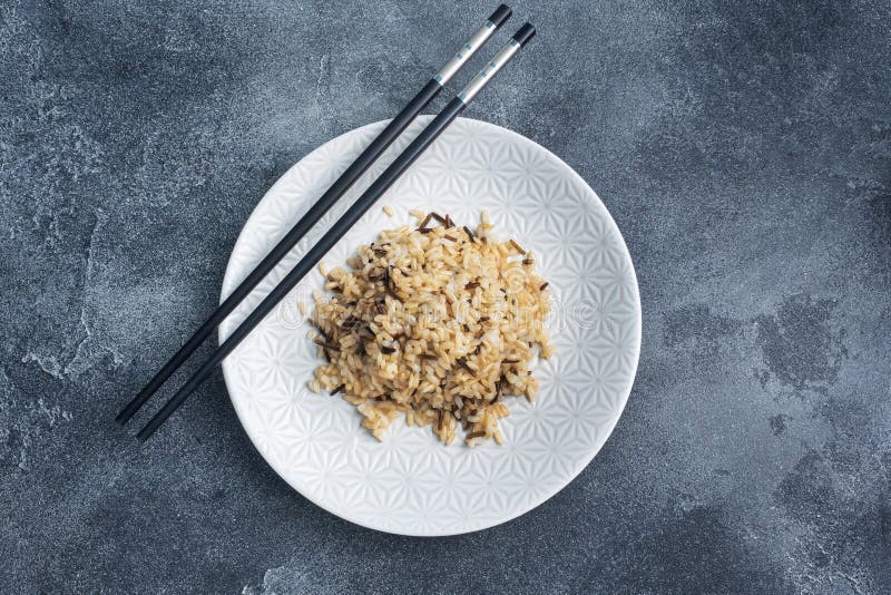 Brown and Unpeeled Rice on a Plate with Chopsticks. Dark Concrete ...