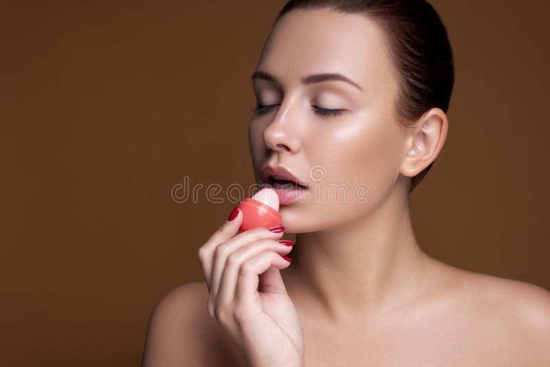 Brunette European Woman Apply Lipstick On Her Lips On Pink Neutral