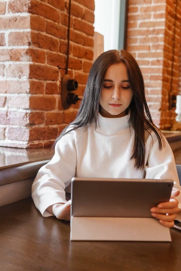 A Brunette Woman is Working on a Tablet at a Table in a Cafe. the Theme ...