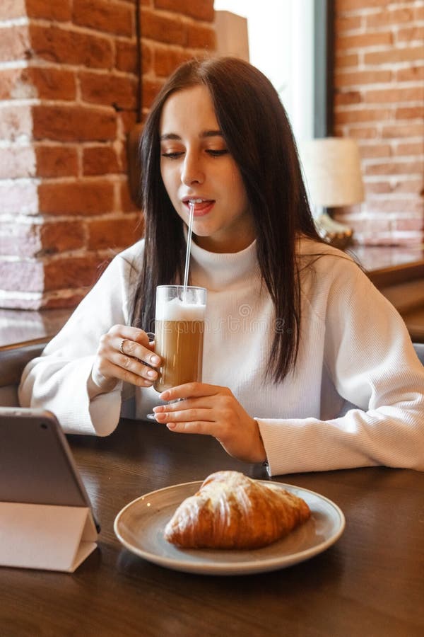 The Brunette is Working with a Tablet at a Table in a Cafe. Drinks ...