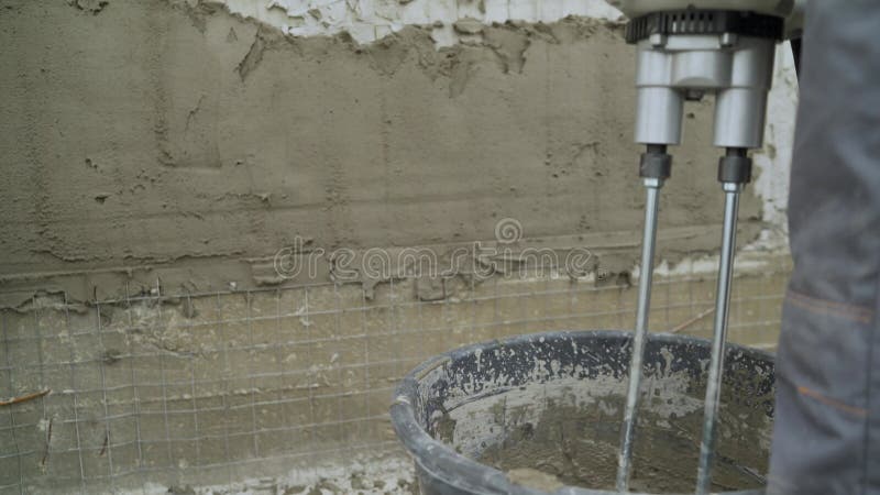 A Worker Mixes a Solution in a Bucket with a Construction Mixer on the ...