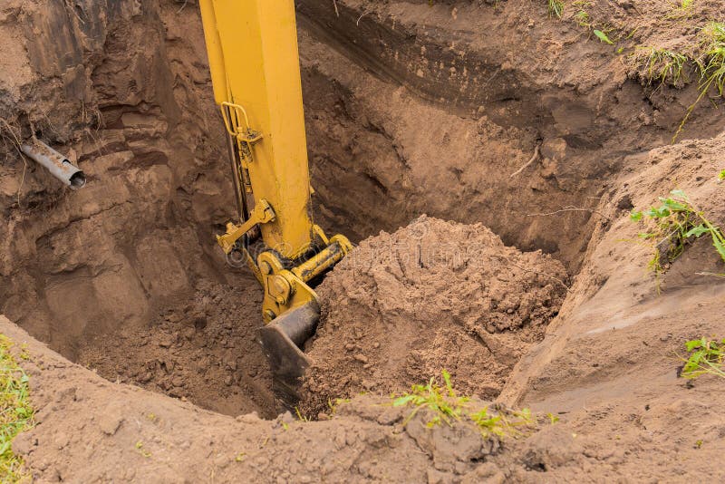 A Bucket of Excavator with a Pile of Earth Digs a Hole on the ...
