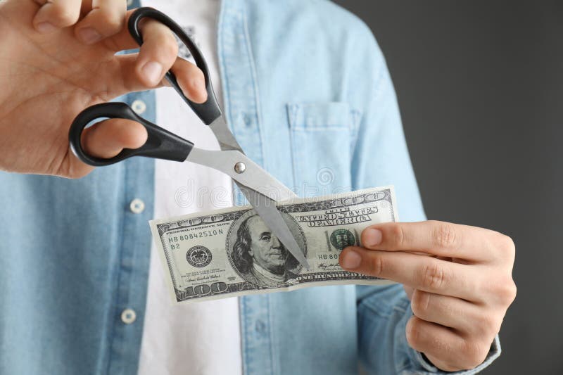 Budgeting. Man Cutting Dollar Banknote with Scissors on Dark Grey ...
