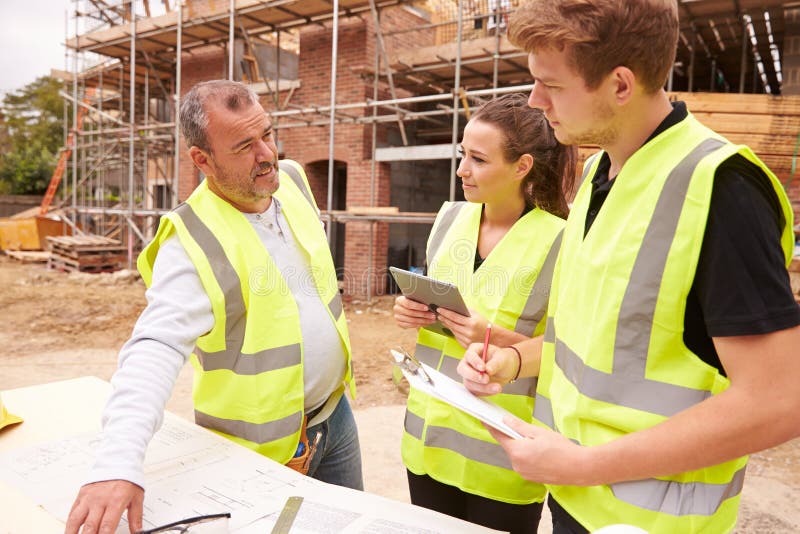Builder on Building Site Looking at Plans with Apprentices Stock Photo ...