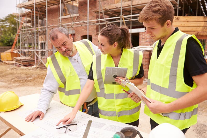 Builder on Building Site Looking at Plans with Apprentices Stock Photo ...