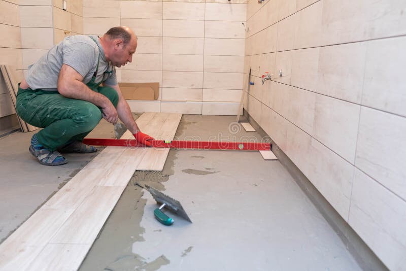 A Builder Checks the Surface Level of Tiles Laid on the Bathroom Floor ...