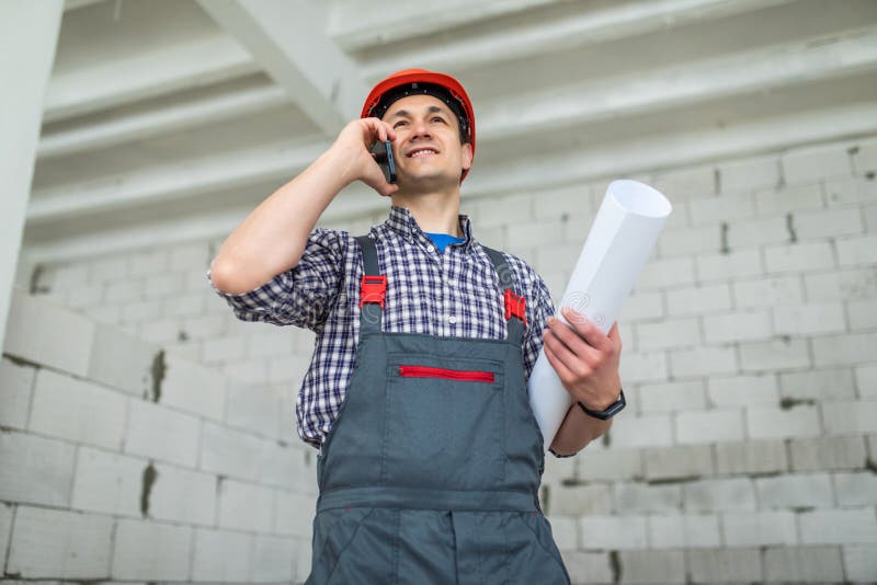 Builder Foreman Talking on His Mobile Phone As he Consults a Blueprint ...