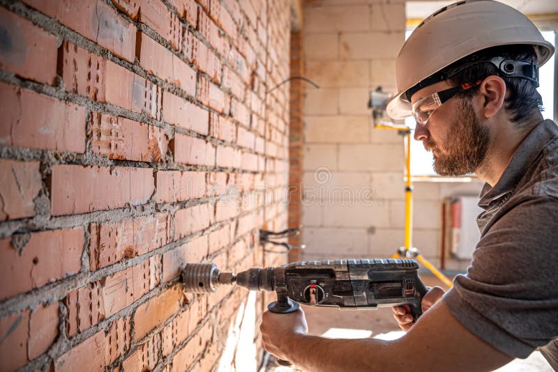 A Builder in a Helmet and Goggles Works with a Drill Stock Image ...