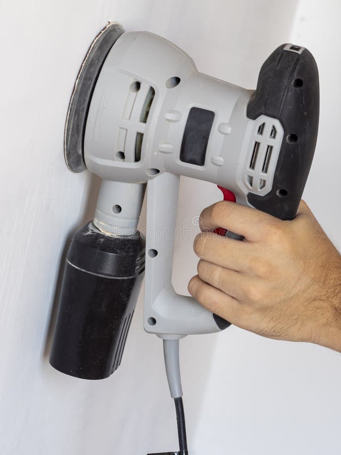 A Builder Uses a Sander To Process a White Concrete Wall. Construction ...