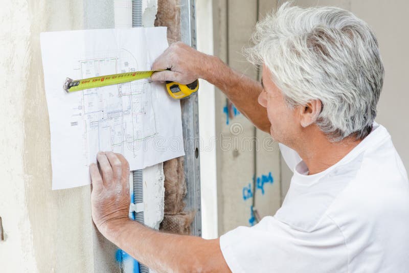 Builder Using Tape Measure To Check Building Plans Stock Photo - Image ...