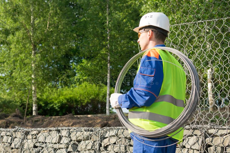 Builder in a White Helmet Carries a Hank of Wire on His Shoulder, Rear ...