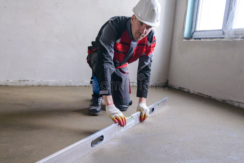 A Builder in Work Clothes is Doing His Job, Leveling the Floor, Pouring ...