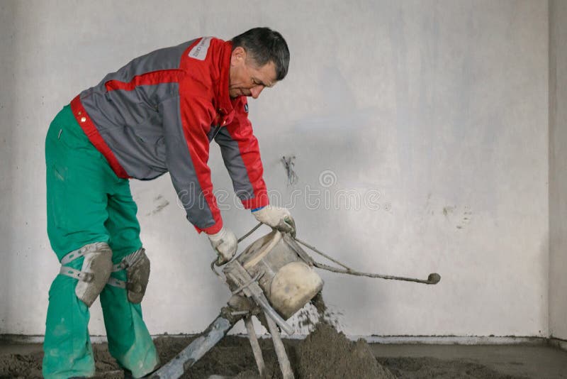 A Builder in Work Clothes is Doing His Job, Leveling the Floor, Pouring ...