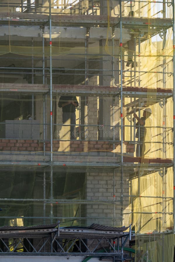 Builders Working Behind Yellow Scaffolding Mesh on a Construction Site ...