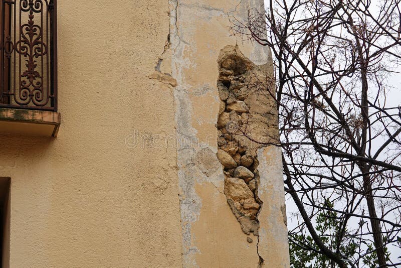 A Building Wall Reveals Damage with Exposed Stones and Peeling Plaster ...
