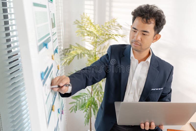 A Business Analyst Examining Charts and Statistics on a Whiteboard, Using Data-driven Insights ...