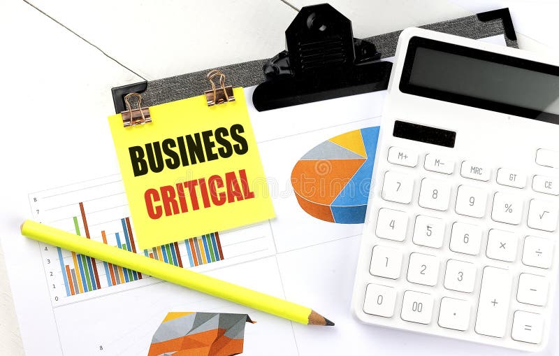 BUSINESS CRITICAL Text on Yellow Sticky with Calculator, Pencil and ...