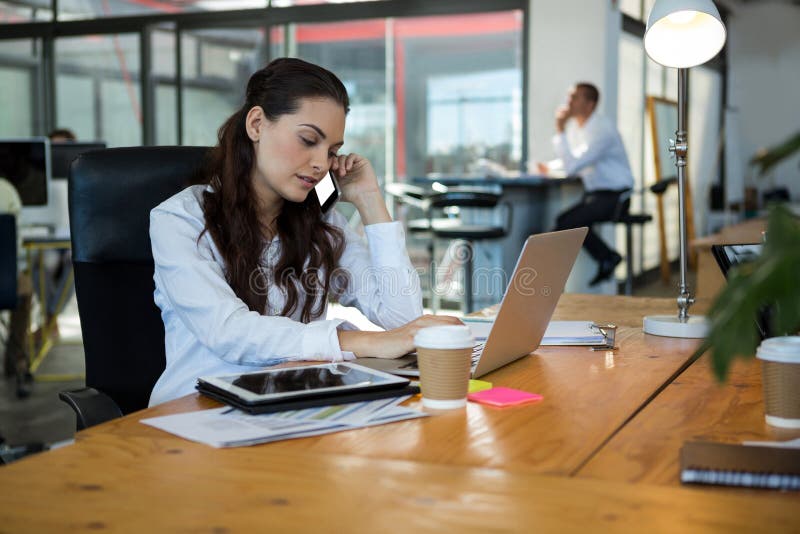 Business Executive Talking on Mobile Phone while Using Laptop at Desk ...
