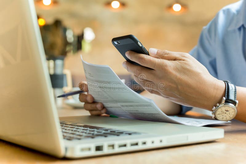 Business Man Using Cell Phone and Holding Document with Laptop on Table ...