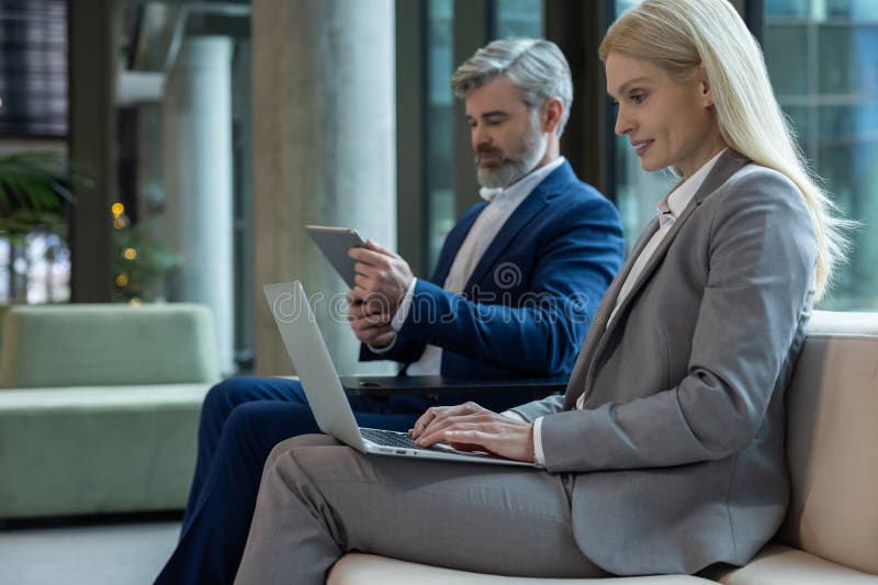Business Partners Sitting in the Hall with Laptops and Working Together ...