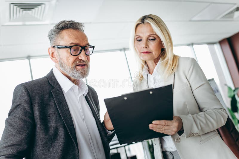 Two Mature Professionals Discussing Documents in a Contemporary Office ...