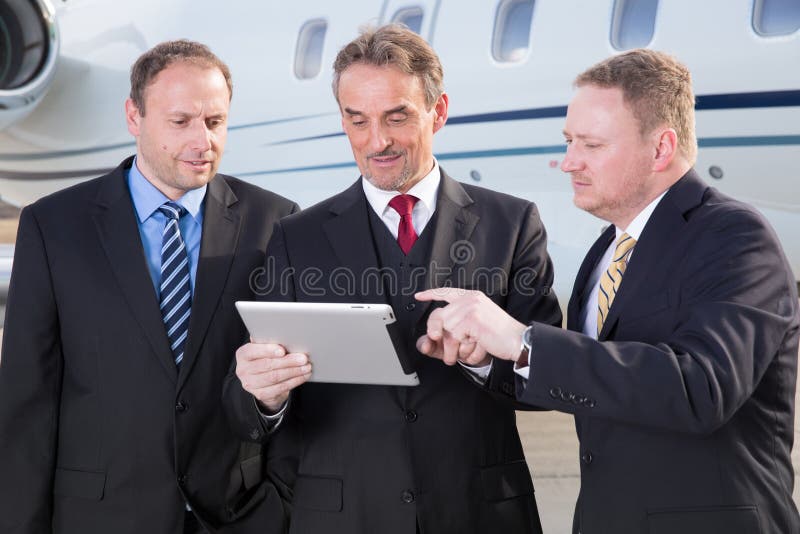 Business Team in Front of Corporate Jet Looking at Tablet Comput Stock ...