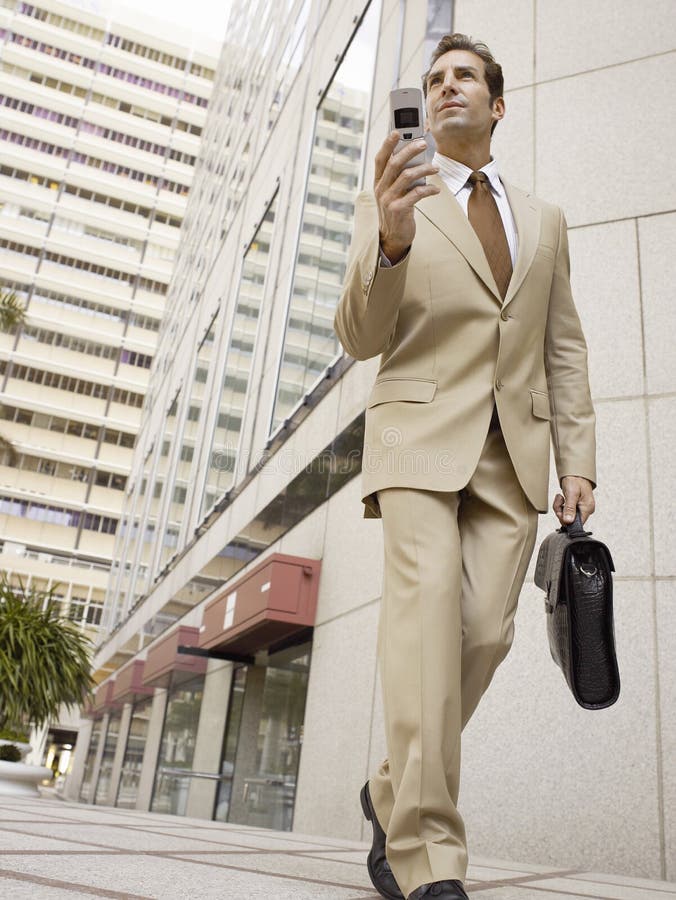 Businessman Holding Mobile Phone while Walking by Office Building Stock ...