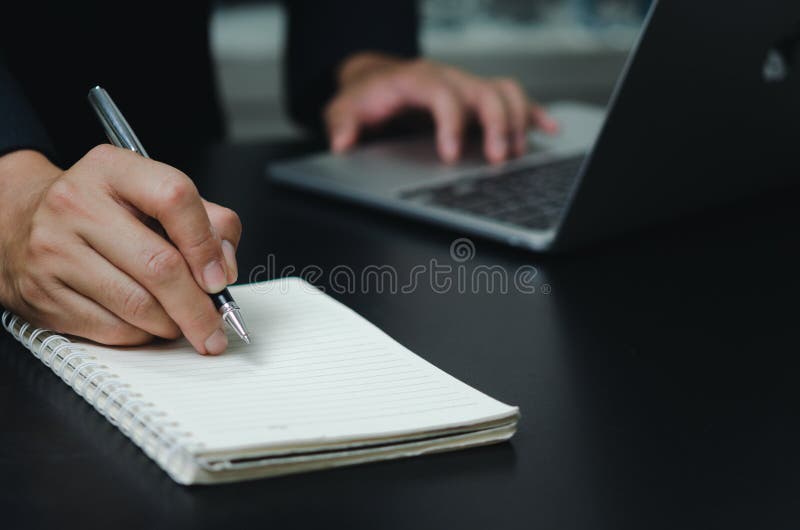 Businessman Holding Pen Writing Book Note on Desk with Computer Laptop ...