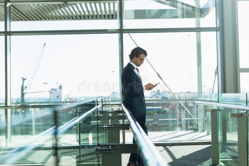 Businessman Leaning on Railing and Using Mobile Phone in Corridor at ...