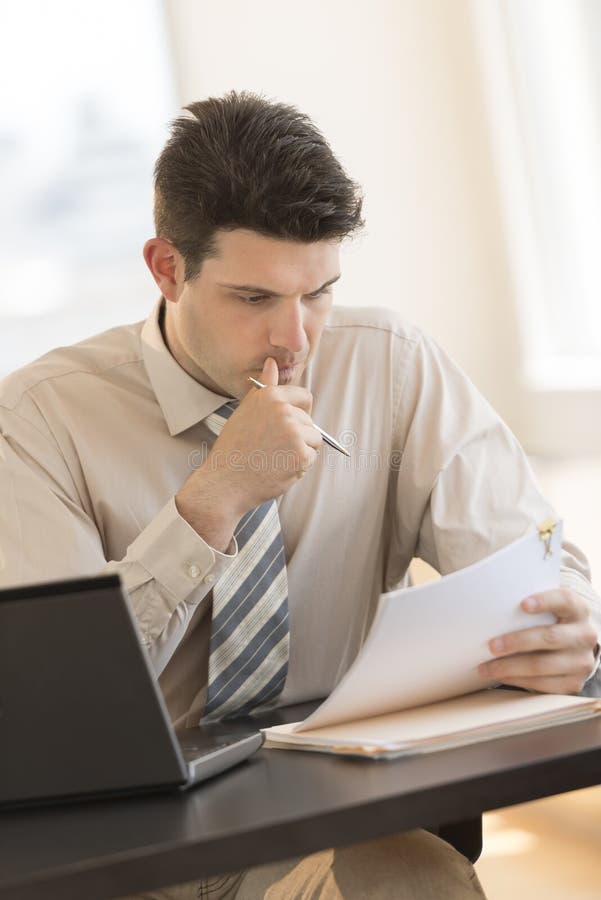Businessman Looking at Documents while Sitting at Desk in Office Stock ...