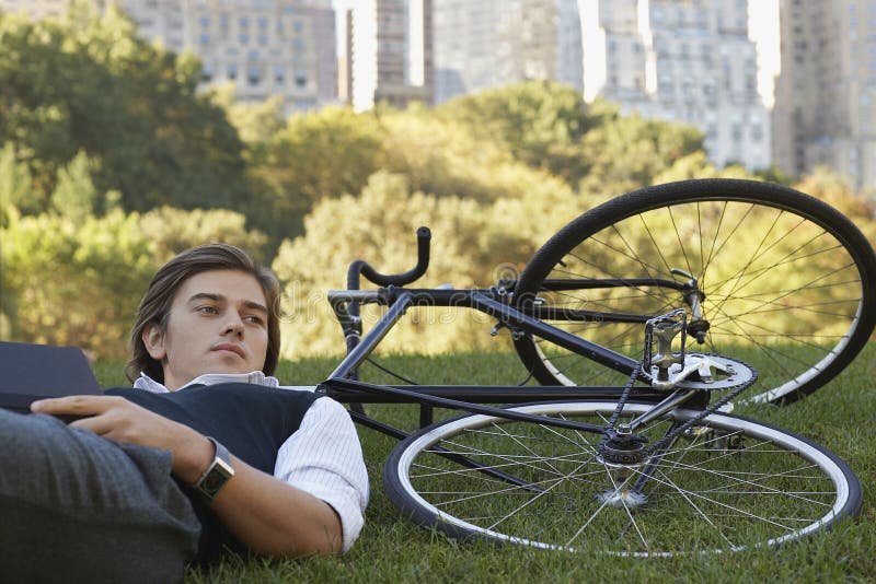 Businessman Lying Down on Bicycle in Park Stock Image - Image of ...