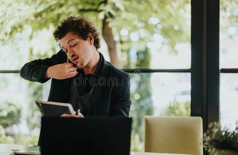 Businessman Multitasking on Phone and Taking Notes at Desk in Modern ...