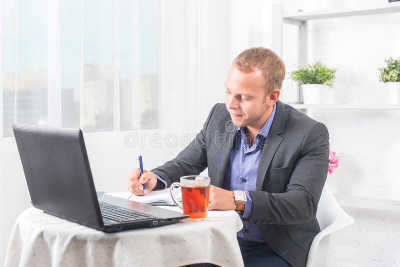 Businessman in Office Sitting at Table with a Laptop Writes ...