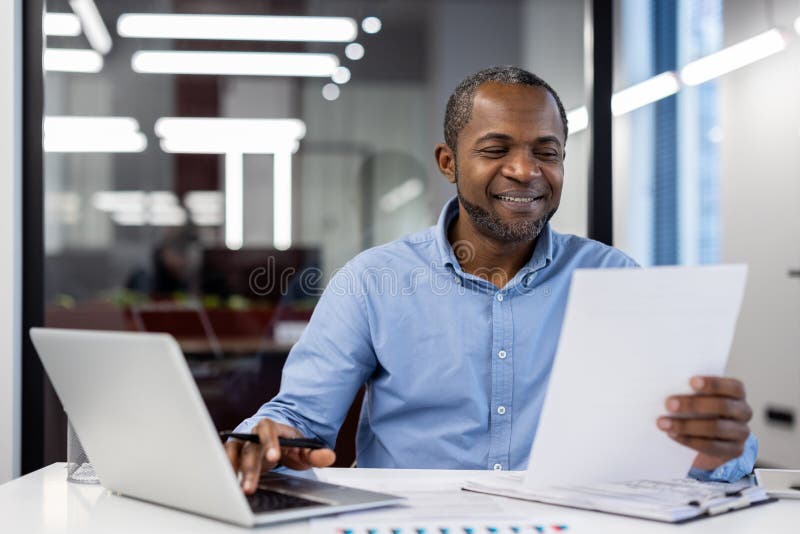 Smiling Businessman Reviewing Documents while Working on Laptop in ...