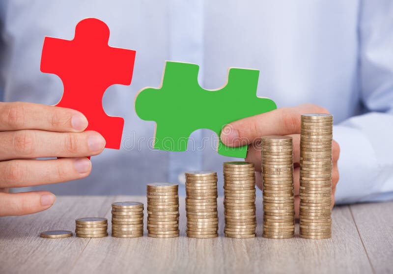 Businessman with Puzzle Pieces and Stacked Coins at Desk Stock Photo ...