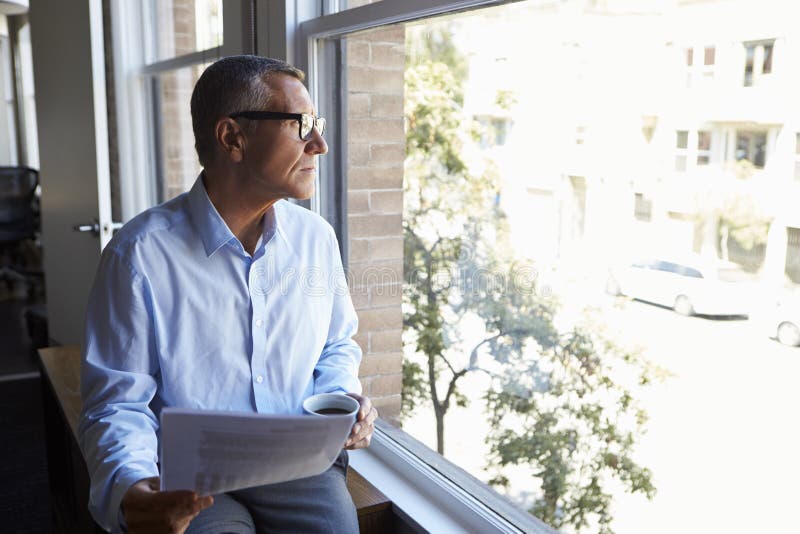 Businessman Reading Document Sitting by Office Window Stock Photo ...