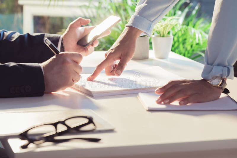 Businessman Signing Documents and Using Smartphone while Colleague ...